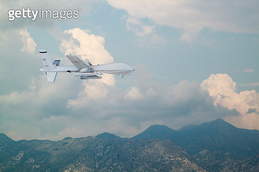 Spy unmanned aerial vehicle (UAV) flies over low mountains in mist with ...