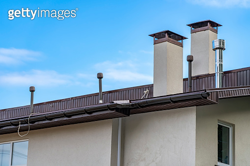 exhaust air pipes and brown rain gutter on private house roof. Metallic ...