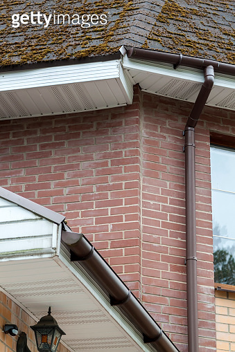 Corner of house with old roof from bituminous tile with moss and rain ...