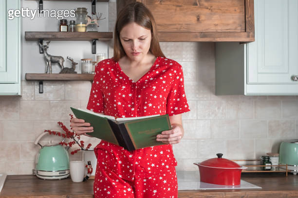 Woman reading recipe book at kitchen interior. Female with cookbook in ...