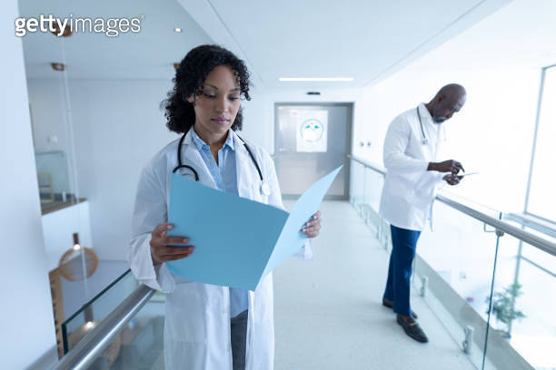 Diverse male and female doctor reading patient file and using digital ...