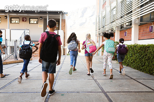 Rear view of group of diverse students with backpacks running at ...