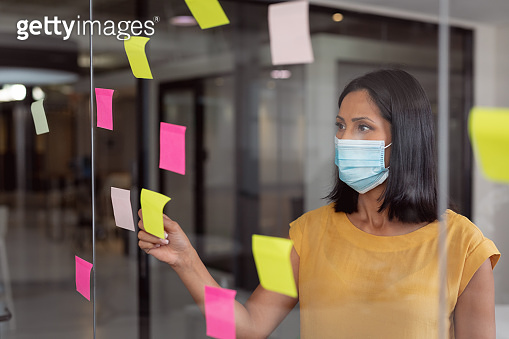 Caucasian businesswoman wearing face mask brainstorming, reading ...