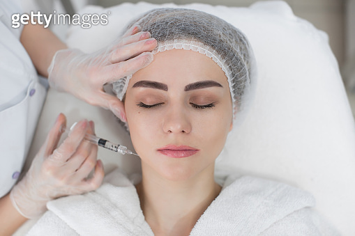 Hands of cosmetologist making injection in face, lips. Young woman gets ...