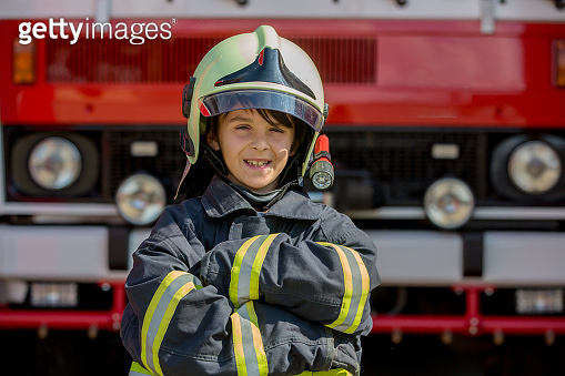 Child, cute boy, dressed in fire fighters cloths in a fire station with ...