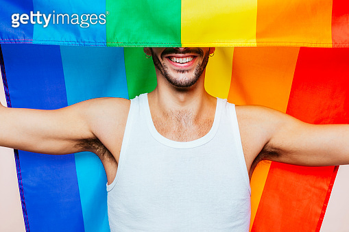 Smiling homosexual man covering half part of his face with a gay pride ...