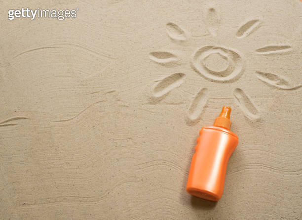Sand texture with painted sun and orange sunscreen tube. Empty space ...