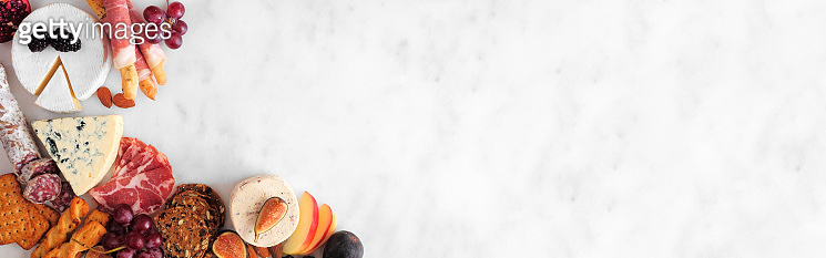 Corner border of assorted cheese and meat appetizers over a white ...