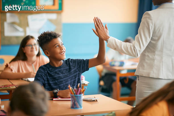 Happy black elementary student and his teacher giving high five during ...