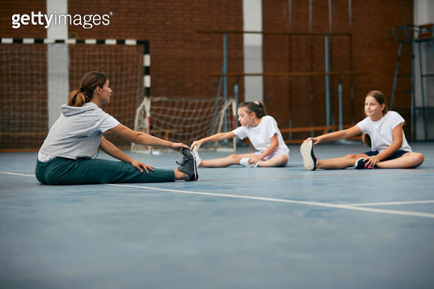 Female coach and elementary students stretching during physical ...