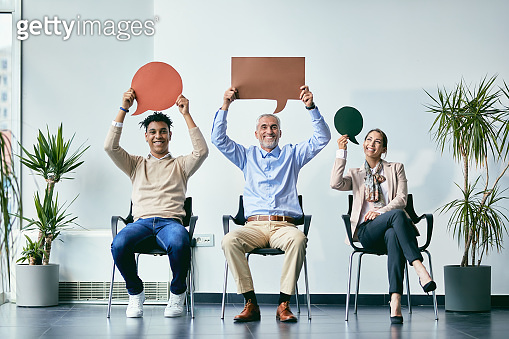 Happy business people holding colorful speech bubbles while sitting in ...