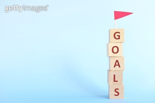 Reach an end goal concept. Wooden blocks with word goal and red flag on ...