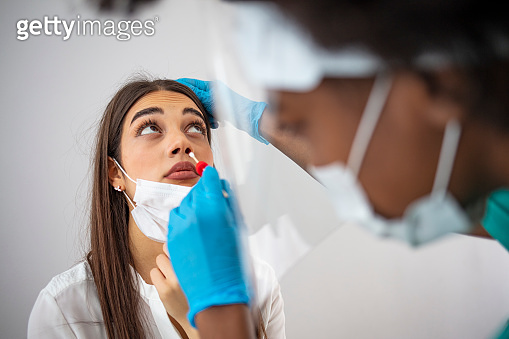 Doctor in protective workwear taking nose swab test from young woman ...