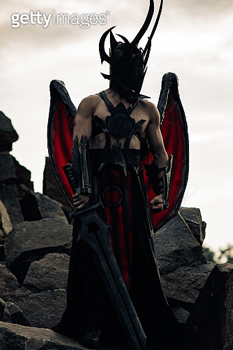 Daemon of death with wings stands with black sword among rocks against ...
