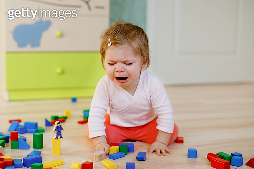 Upset crying baby girl with educational toys. Sad tired or hungry alone ...