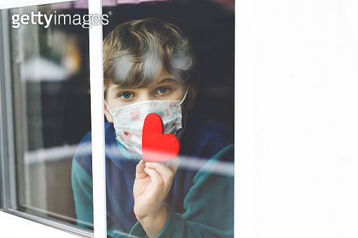 Lovely little school kid boy by a window wearing medical mask and ...