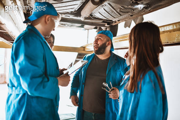 Mechanic Putting Tongue Out And Joking With Apprentices Under Car In ...