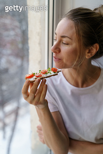Woman eating rye crisp bread with creamy vegetarian cheese tofu, tomato ...