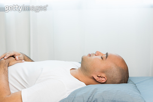 An Asian bald man around the age of 30 in a white T-shirt is sleeping ...