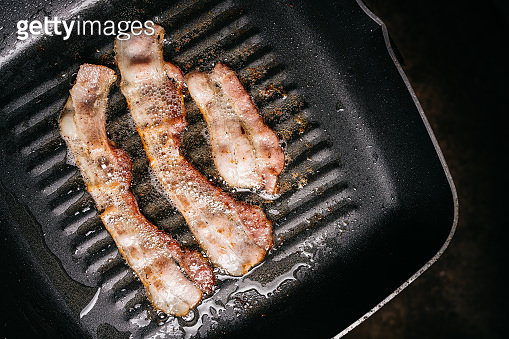 Top view of frying sizzling bacon strips in a pan with hot greasing ...