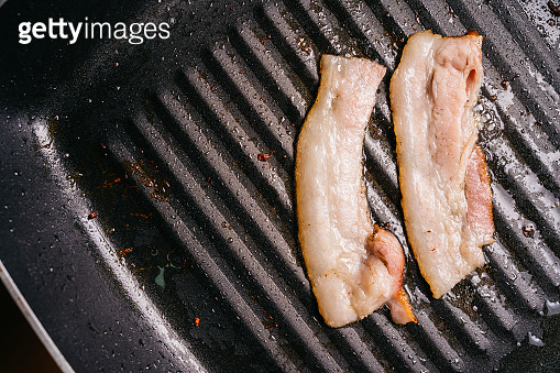 Top view of frying sizzling bacon strips in a pan with hot greasing ...