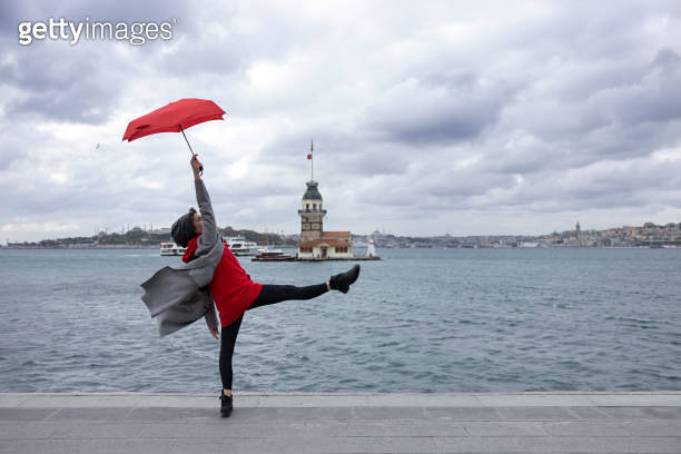 Dancer woman running in wind in front of maiden tower with red umbrella ...
