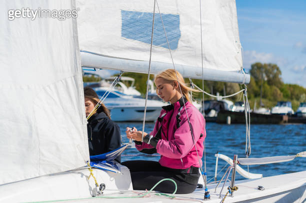 On the pier, two pretty girls pull sails on a boat to participate in a ...