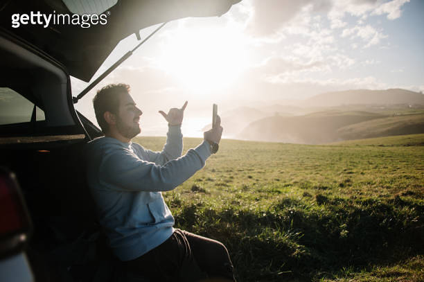 Young man video calling in a beautiful landscape 이미지 (1300287350) - 게티이미지뱅크
