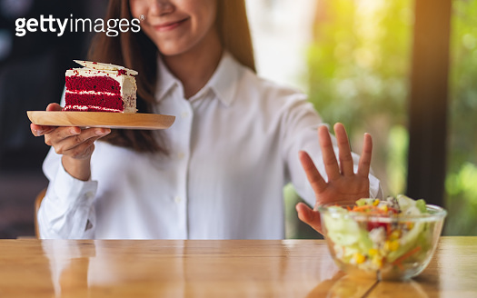 A woman choosing to eat cake and making hand sign to refuse vegetables ...
