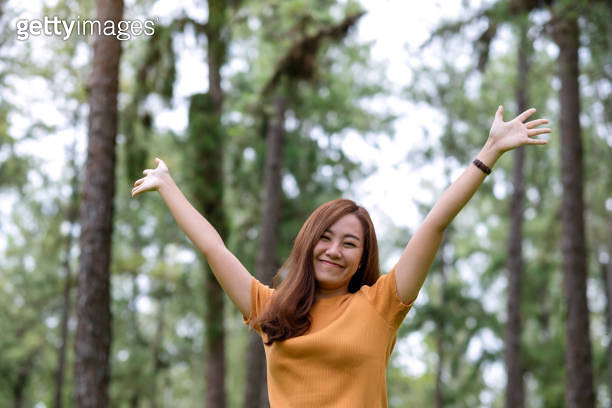 Portrait image of a happy woman with arms rising in the park ...