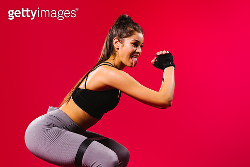 A girl with a pumped-up figure squats with a resistance elastic band ...