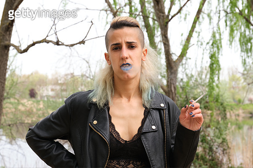 Young punk woman smoking a cigarette in a park. Rock and roll lifestyle ...
