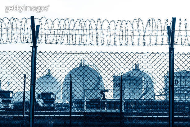 Steel fence, topped with razor wire, protecting a fuel storage facility ...