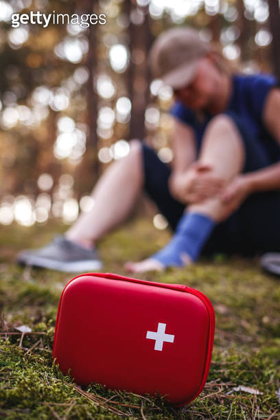 First aid kit and defocused injured woman with sprain ankle in woodland ...