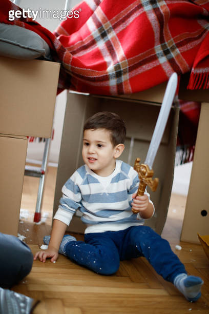 Toddler sitting with toy sword in front of the boxes and defending his ...