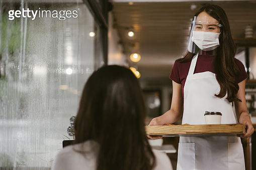 Asian waitress with face protective mask and face shield serving coffee ...