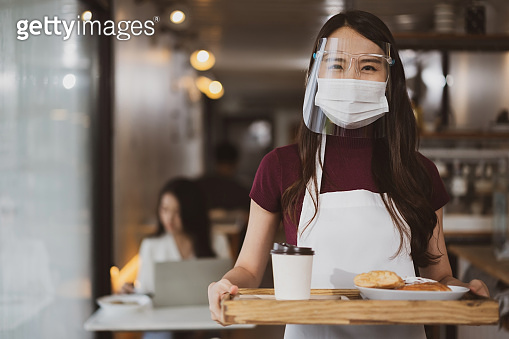 Asian waitress with face protective mask and face shield serving coffee ...
