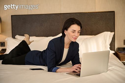 Beautiful young Caucasian business woman lying down on a bed in a hotel ...