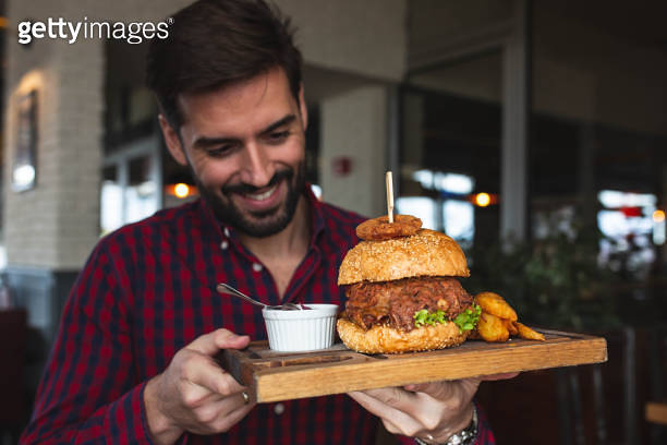 Handsome man holding a big burger with smile on his face 이미지 ...