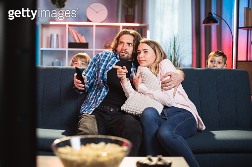 Frightened family sitting on couch and watching horror movie ...