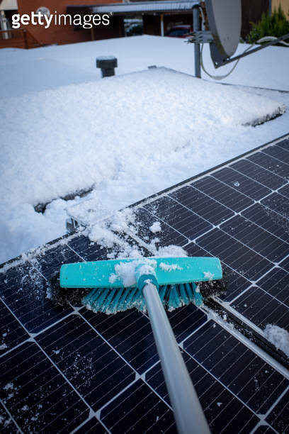 Solar panels of a photovoltaic system on a roof are cleared of snow ...