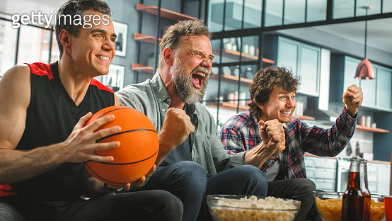 At Home Three Happy Basketball Fans Sitting on a Couch Watch Game on TV ...