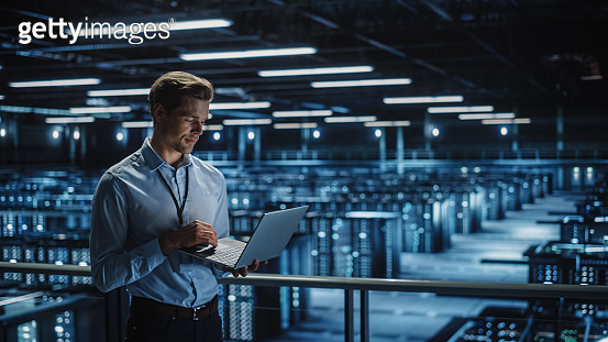 Data Center Specialist Engineer Using Laptop Computer. Server Farm Cloud Computing Facility with ...