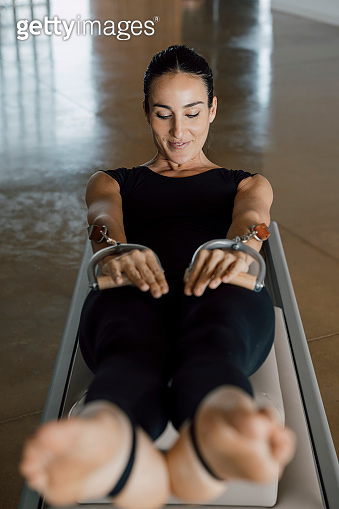 Front view of fit woman pulling strings of a pilates reformer machine ...
