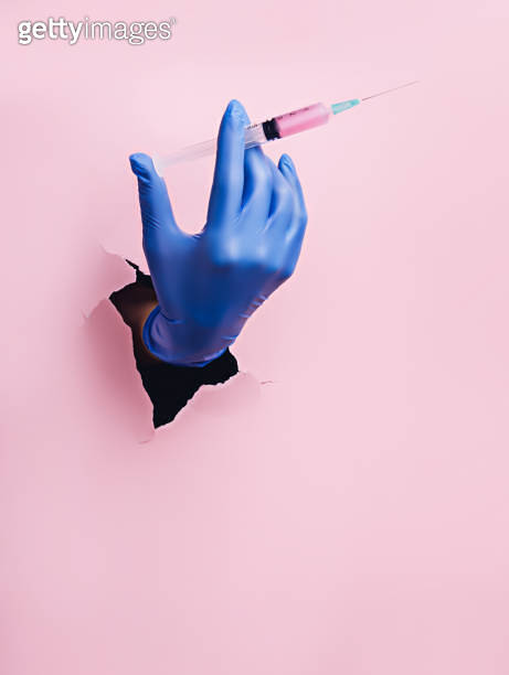 Hand with syringe breaking in through a black hole on yellow background ...