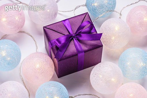 Gift in a shiny purple box and glowing Christmas balls. Festive mood ...