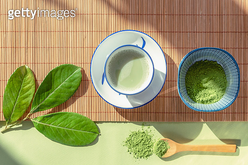 Green matcha tea in a white cup, tea powder and wooden spoon on bamboo ...