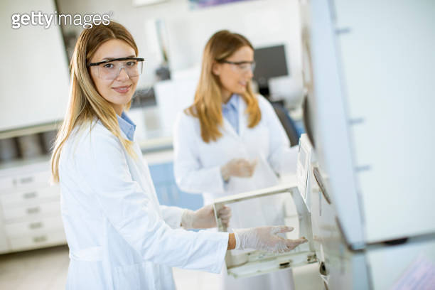 Female scientists in a white lab coat putting vial with a sample for an ...