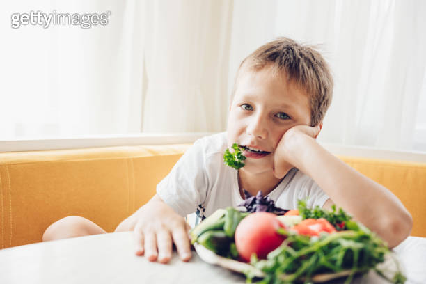 Boy sitting in the kitchen eating healthy vegetables cucumber and ...