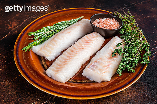 Raw Haddock loin fillet fish on rustic plate with thyme and salt. Dark ...